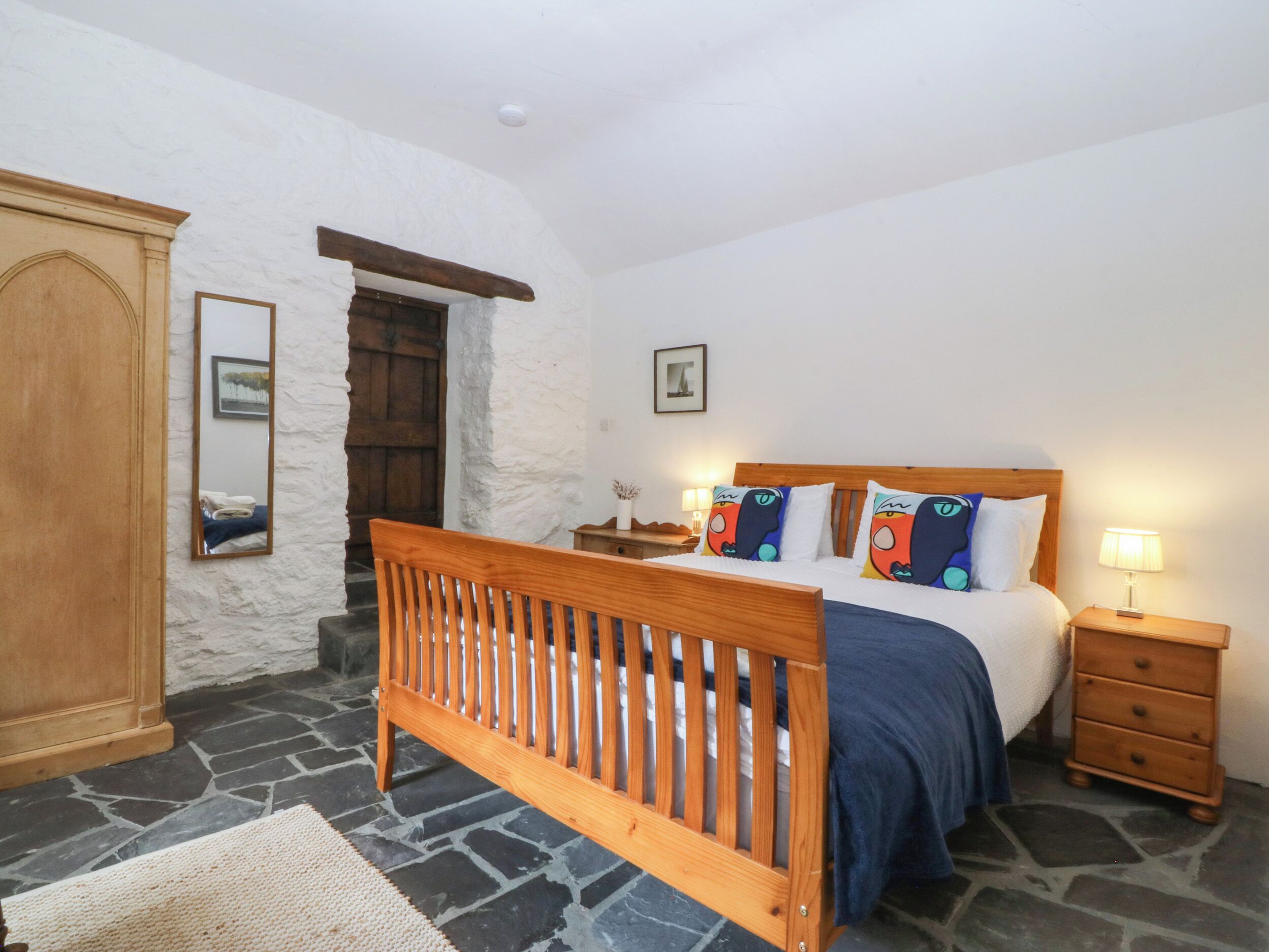 Quarto com cama de madeira, mesa de cabeceira, penteadeira e chão de pedra.