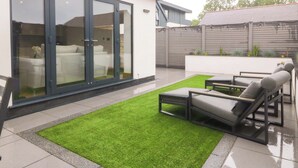 Uma casa moderna com uma ampla porta de vidro deslizante que dá para um pátio com gramado verde e mobiliário de exterior.