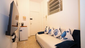 Quarto pequeno e compacto com sofá, televisão, frigorífico e janela com persianas.