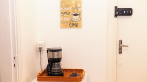 Uma cafeteira em cima de um eletrodoméstico branco, uma bandeja de vime e um painel de parede com texto sobre café.