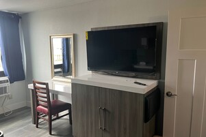 Quarto com televisão presa a um móvel, uma cadeira e uma janela com cortinas.