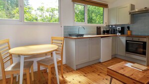 Uma cozinha compacta com área de refeições, piso de madeira e janelas amplas com vista para o verde.