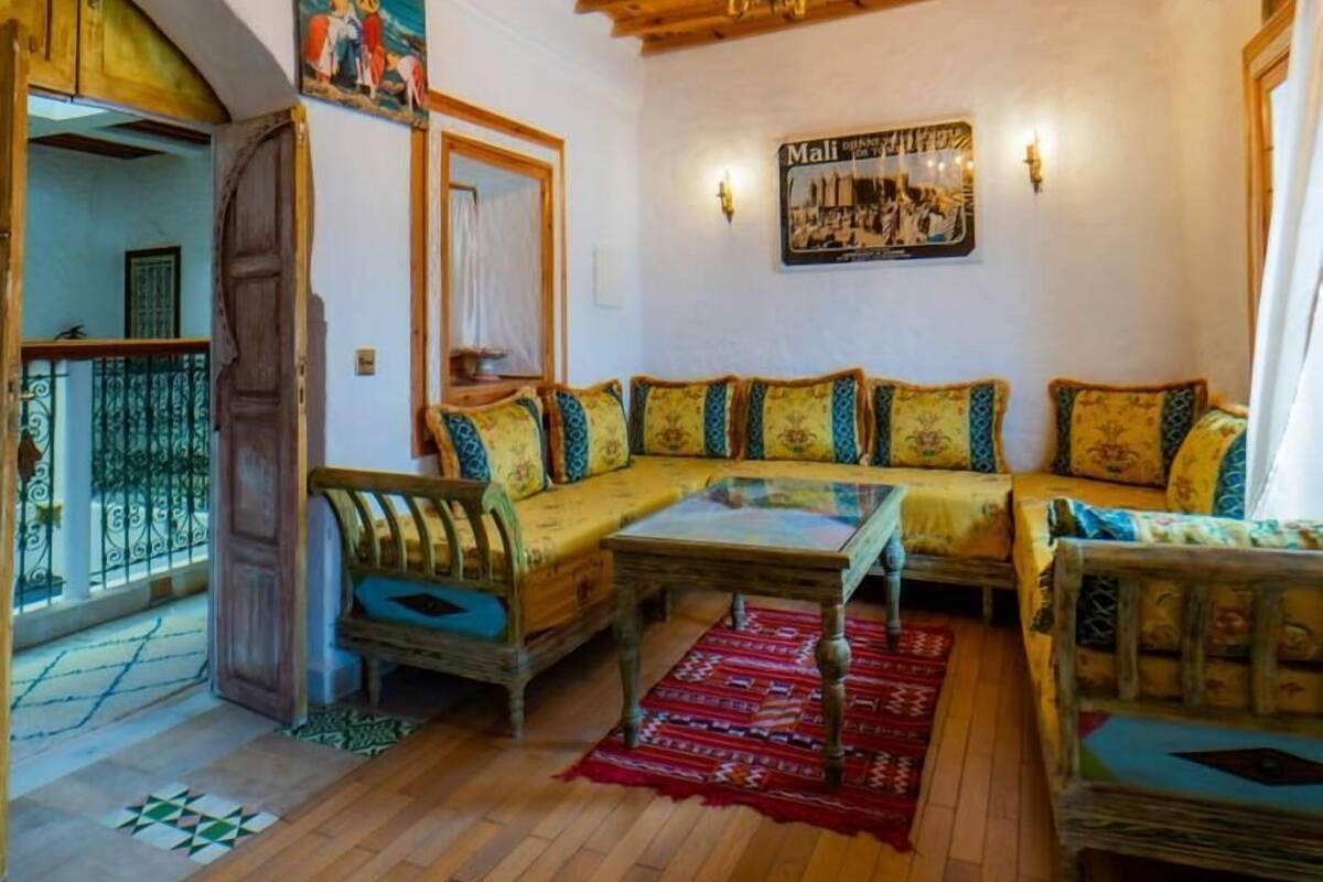 Uma sala de estar aconchegante com vigas de madeira, um conjunto de sofás e um tapete estampado.
