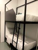 Uma cama beliche com escada, roupa de cama branca e uma pequena prateleira com abajur e um livro.