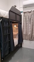 Uma cama beliche com cortinas, uma luminária de cabeceira e um aparelho de ar condicionado.