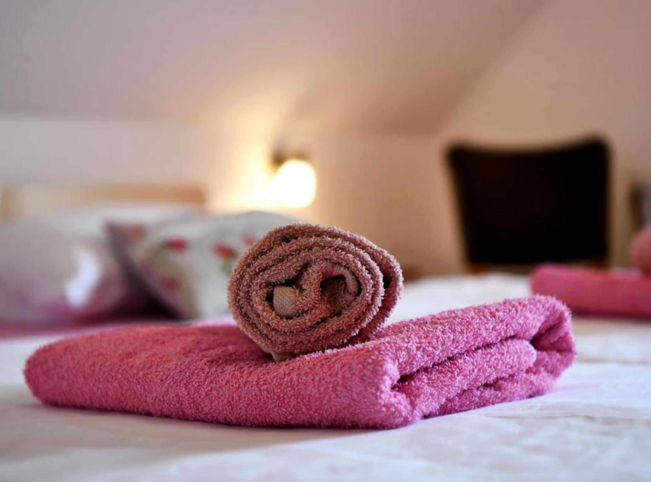 Cama bem arrumada com toalhas cor-de-rosa e uma toalha enrolada por cima.