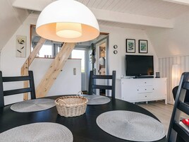 Uma área de refeições com uma mesa preta, jogos americanos cinzas, uma cesta de palha e um teto branco com uma luminária grande.