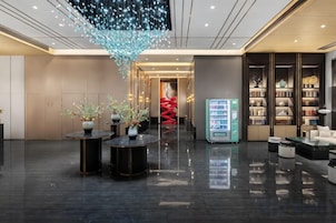 Um lobby moderno com um lustre central, uma máquina de venda automática e uma estante de livros.