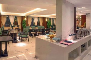 Um saguão de hotel com sofás e poltronas, balcão de recepção e espaço para café.