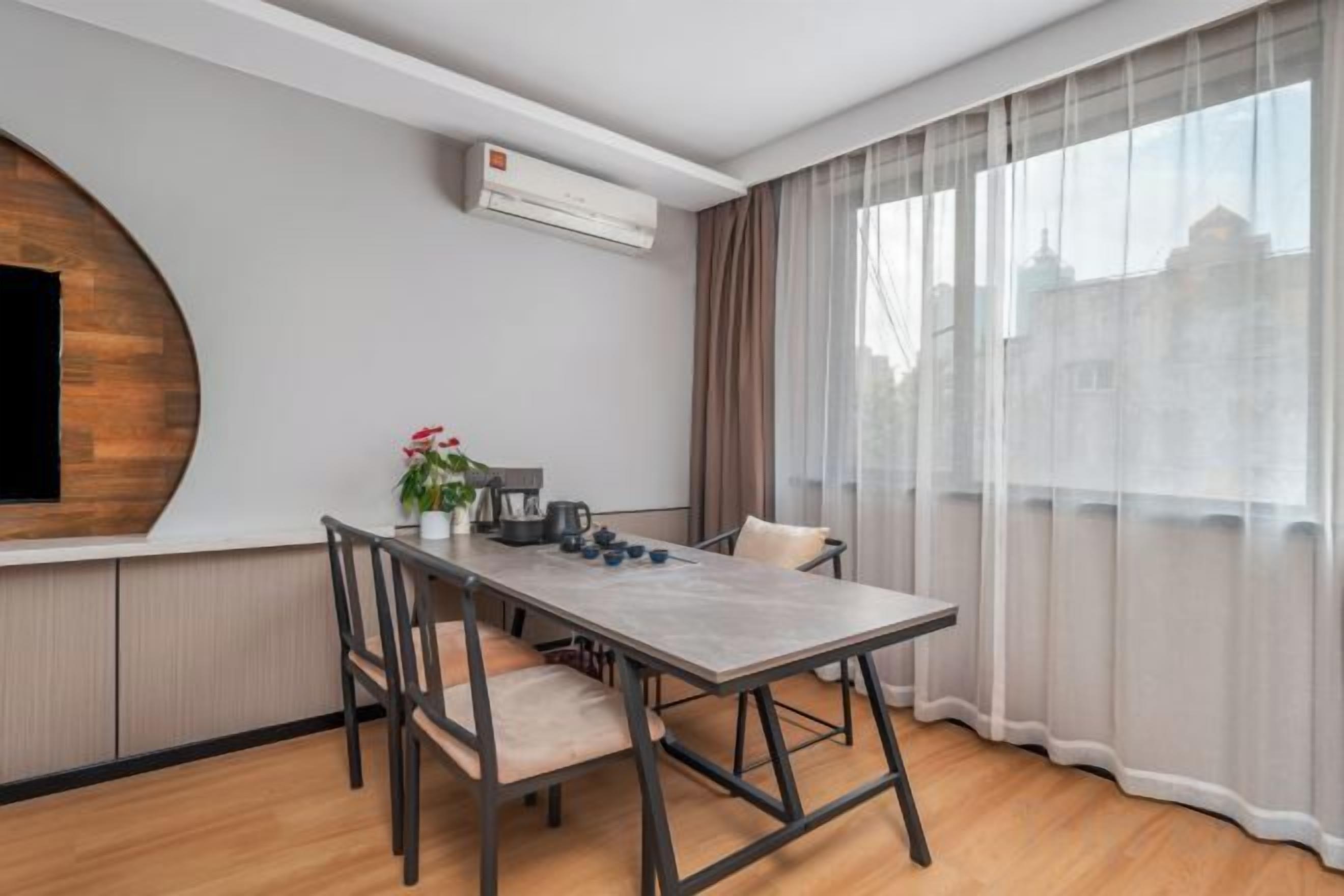 Quarto de hotel moderno com mesa de jantar, cadeiras, TV de tela plana e uma janela grande com cortinas.