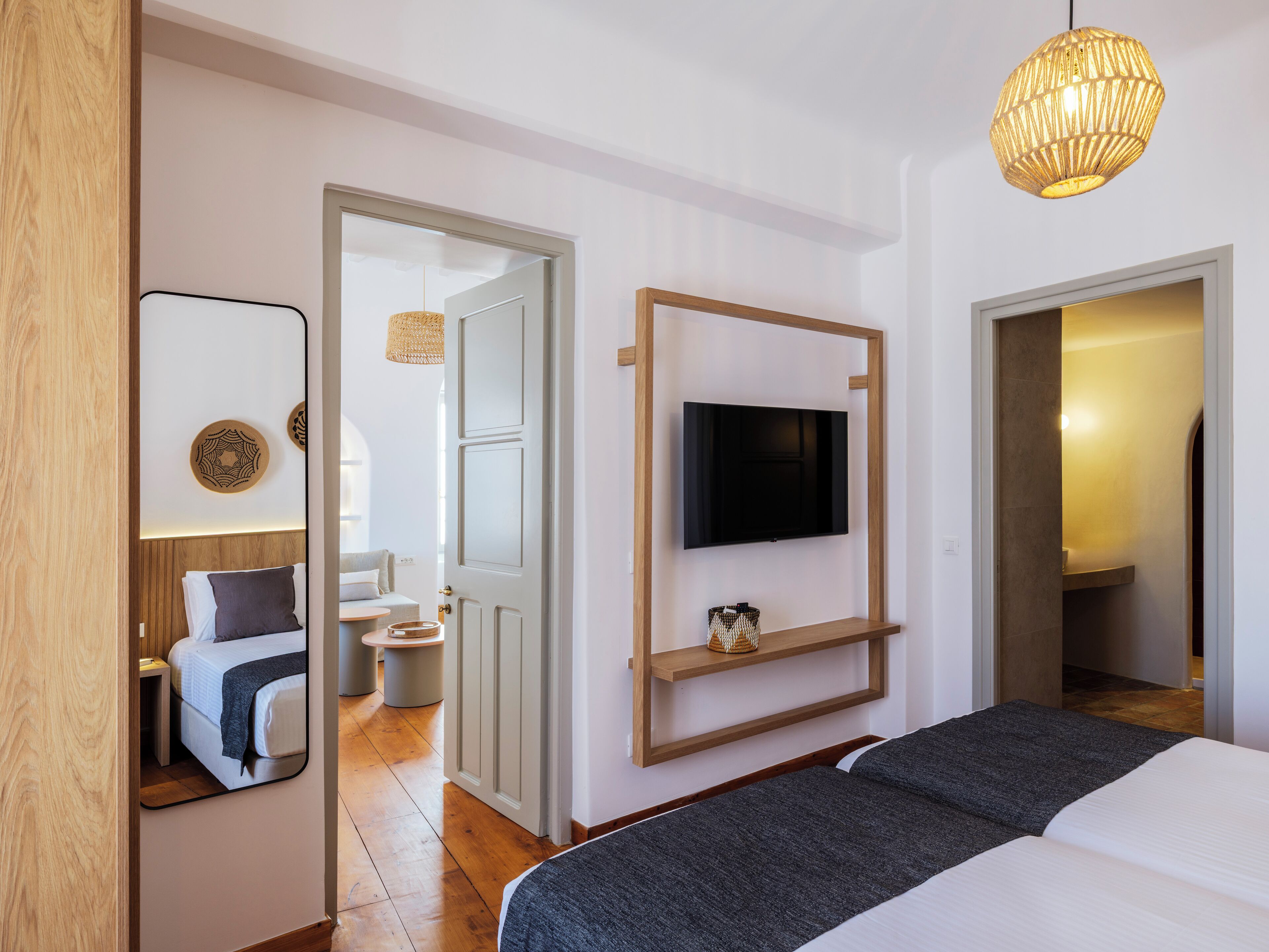 Quarto de hotel com cama, televisão na parede, espelho e porta de madeira.