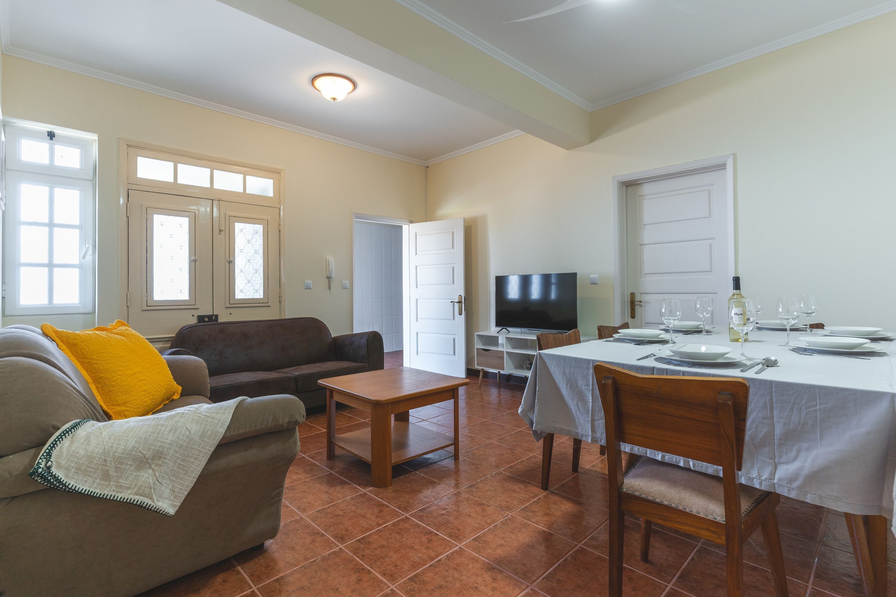 Sala de estar com sofá, mesa de centro e área de jantar com mesa posta para quatro.
