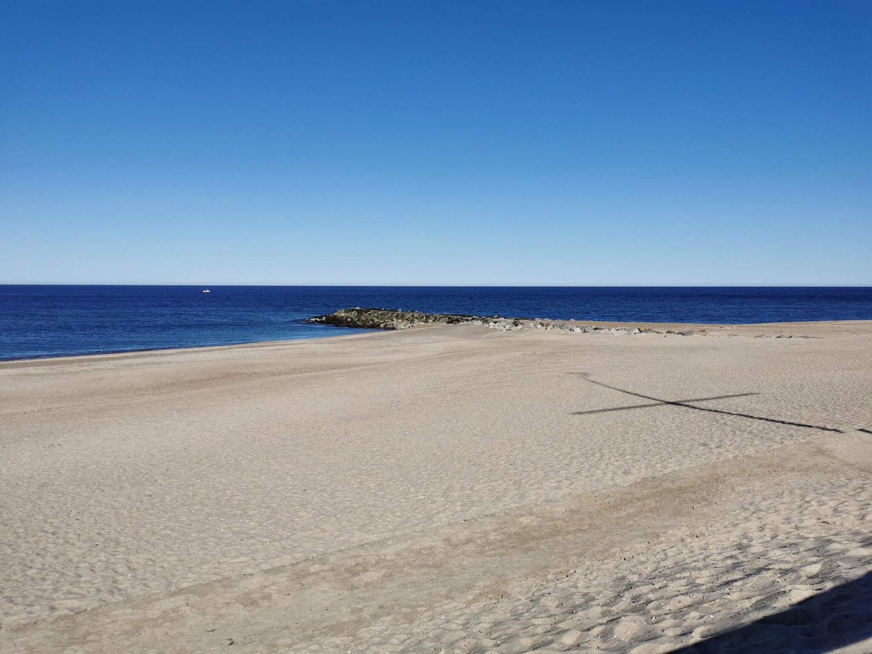 Uma praia arenosa com céu claro e mar calmo.