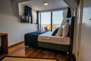 Quarto com cama, televisão, vista para o mar e janela com cortinas.