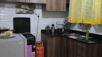 Uma cozinha compacta com armários de madeira escura, fogão a gás, geladeira e cortina amarela.
