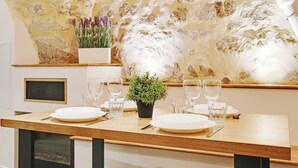 Mesa de jantar posta com pratos, copos e talheres, com uma planta em vaso e um painel decorativo ao fundo.