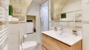 Casa de banho moderna com parede em pedra, lavatório branco e toucador de madeira.