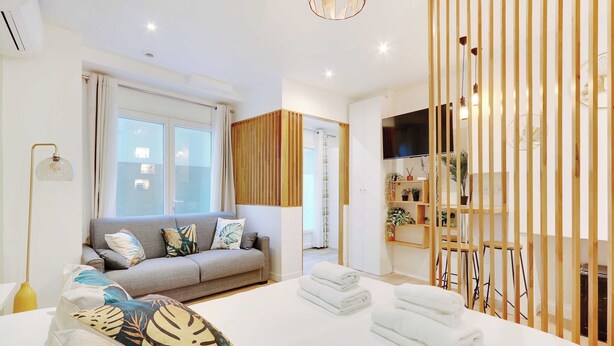 Quarto de hotel moderno com sofá, cama e toalhas dobradas, divisória de madeira e televisão em um suporte.