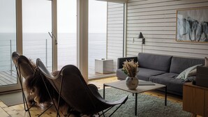 Uma sala de estar moderna com vista para o oceano, um sofá cinzento, uma mesa de centro com um vaso e um piso de madeira.