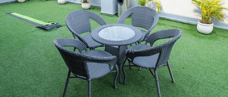 Um terraço no telhado com grama sintética, móveis de vime e plantas em vasos.