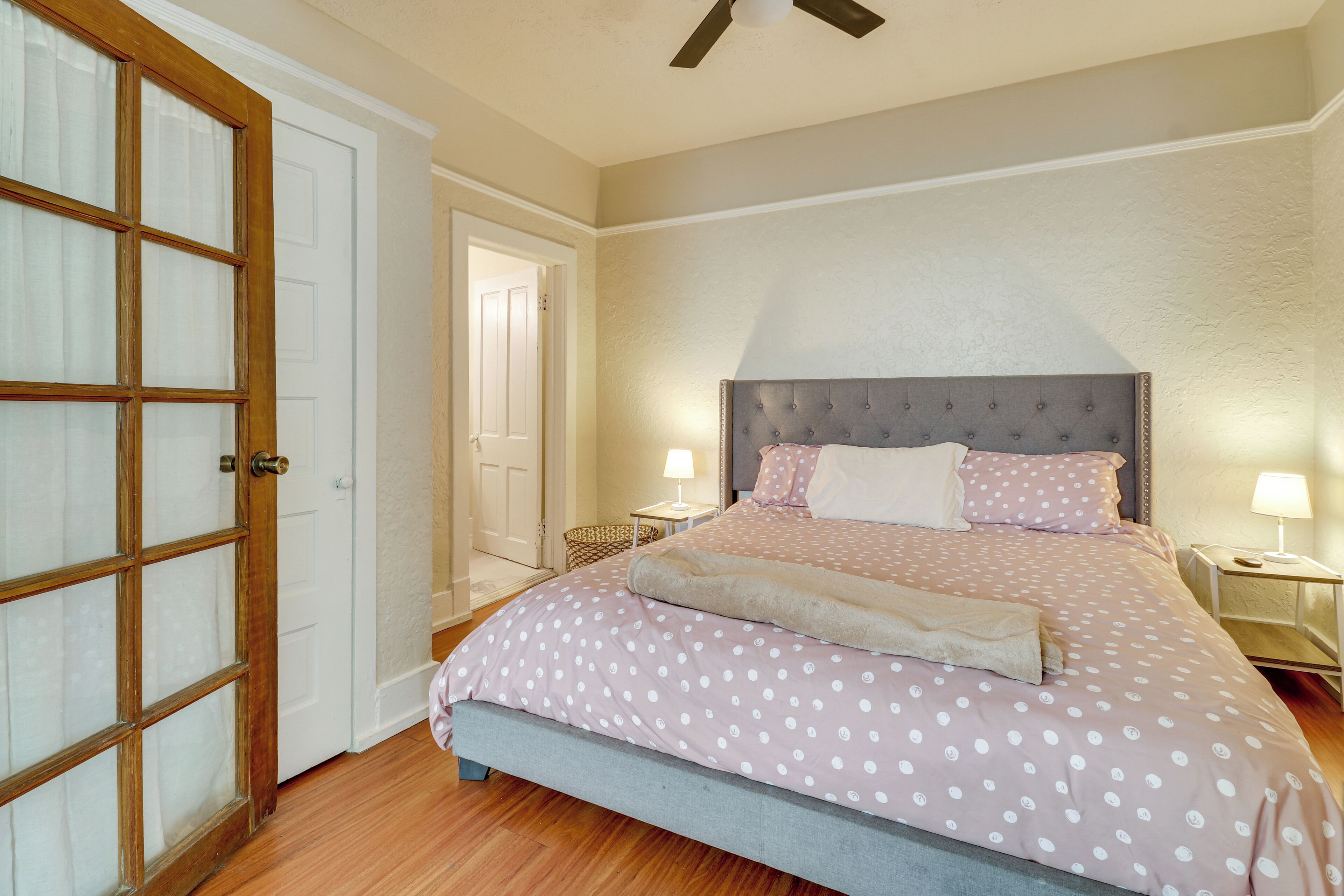 Quarto com cama grande, porta de madeira, ventoinha no teto e duas luminárias de cabeceira.
