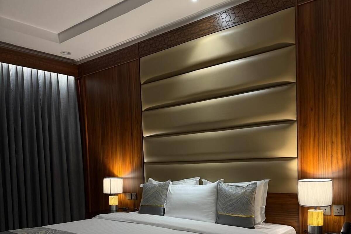 Quarto de hotel moderno com uma cama grande, cabeceira de madeira e duas mesas de cabeceira com abajures.