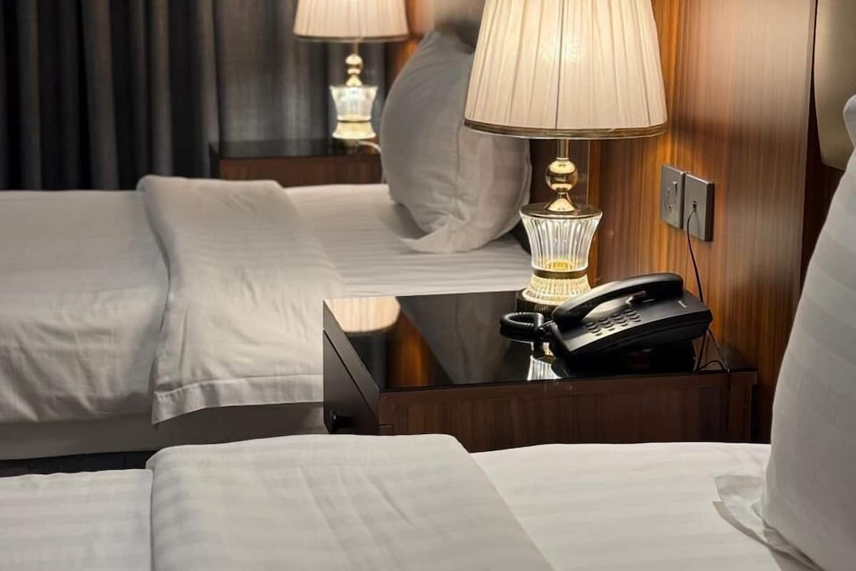 Quarto de hotel com duas camas, uma mesinha de cabeceira com luminária e um telefone.
