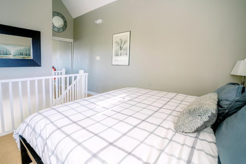 Quarto com cama, corrimão branco, quadro na parede e luminária.