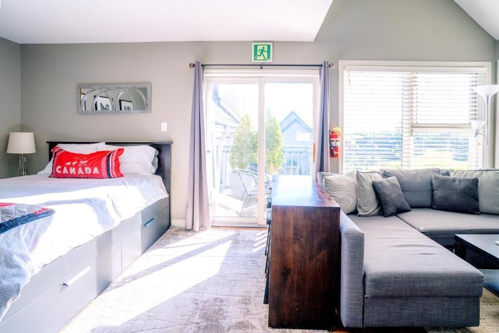 Quarto de hotel com cama, sofá, mesa de centro de madeira e vista para o exterior através de uma porta de vidro.