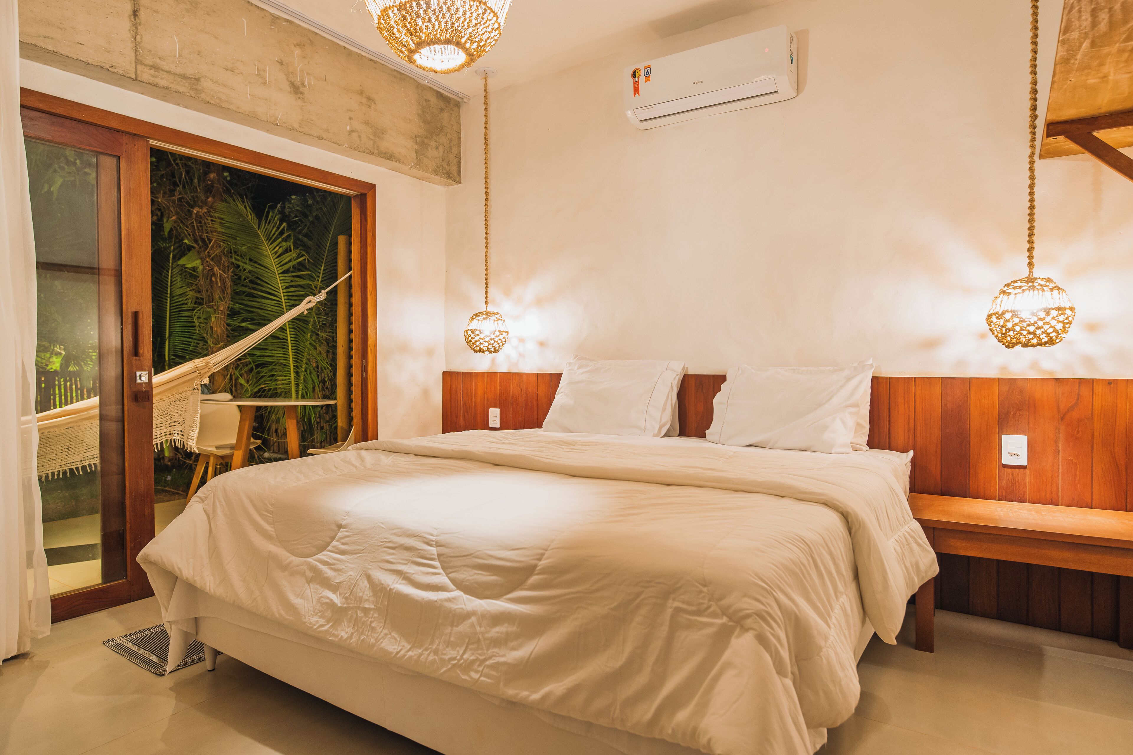 Quarto com cama grande, cabeceira de madeira e duas luminárias pendentes.