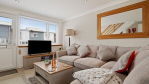 Uma sala de estar moderna com uma TV de tela plana, uma mesa de centro de madeira, um sofá e um espelho grande na parede.