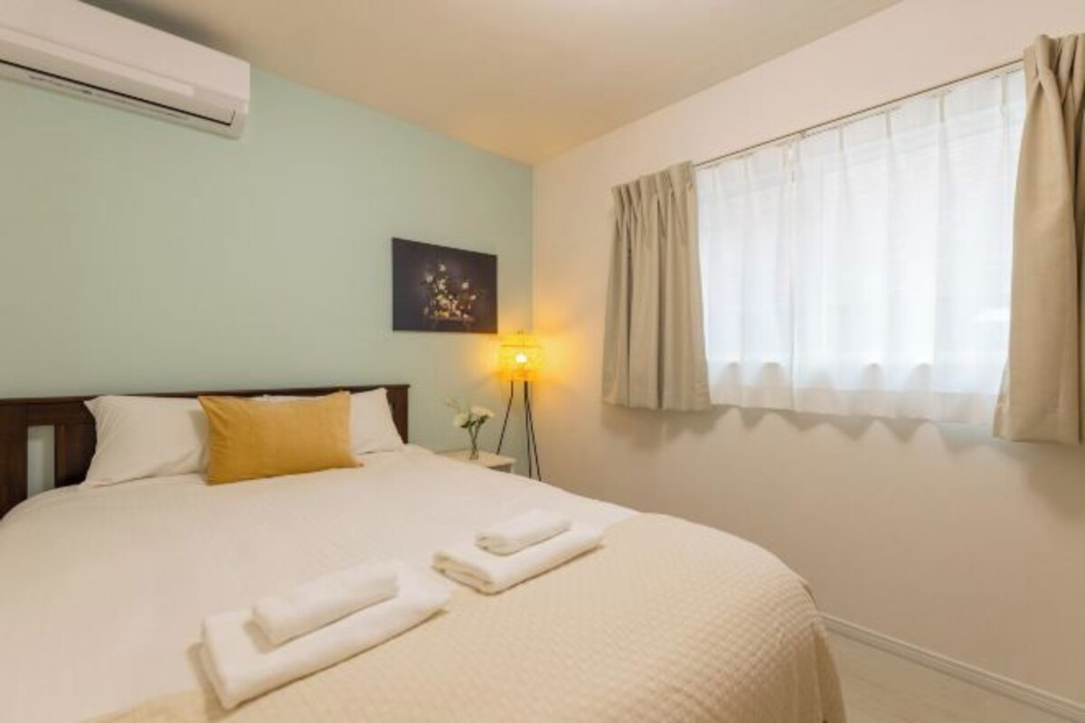 Quarto de hotel com cama, mesa de cabeceira com abajur, quadro na parede e janela com cortinas.