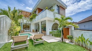 Uma casa moderna com piscina, duas espreguiçadeiras e vegetação exuberante.