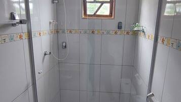 Casa de banho pequena, com azulejos, chuveiro, sanita e uma pequena janela.