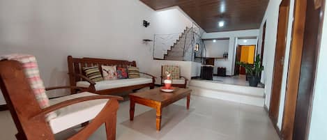 Uma sala de estar com um sofá e uma cadeira de madeira, uma mesa de centro e uma escada que leva a outro cômodo.