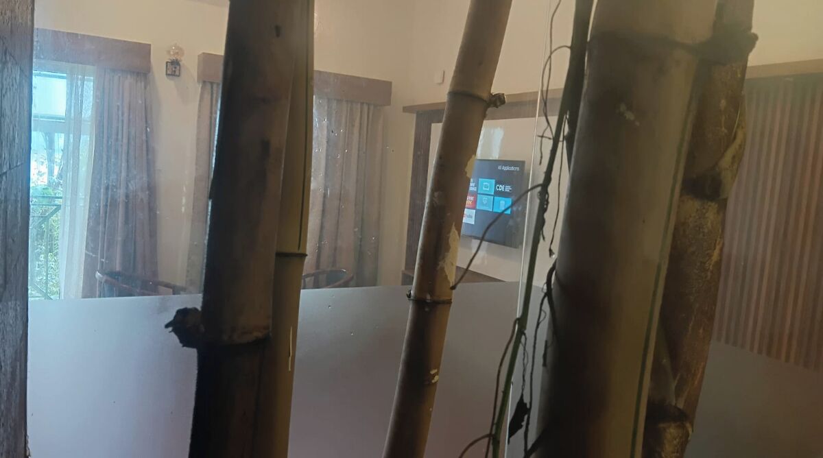 Quarto com pilares de bambu, uma janela grande com cortinas e vista para o exterior.