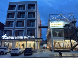 Hotel com fachada moderna, restaurante com área externa e escadaria que leva aos andares superiores.