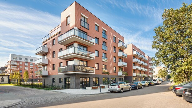 Um edifício de apartamentos com várias andares, varandas, área de estacionamento e céu claro.