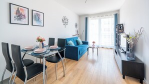 Uma sala de estar moderna com área de refeições, apresentando um sofá azul, cadeiras pretas, uma mesa de vidro e obras de arte emolduradas na parede.