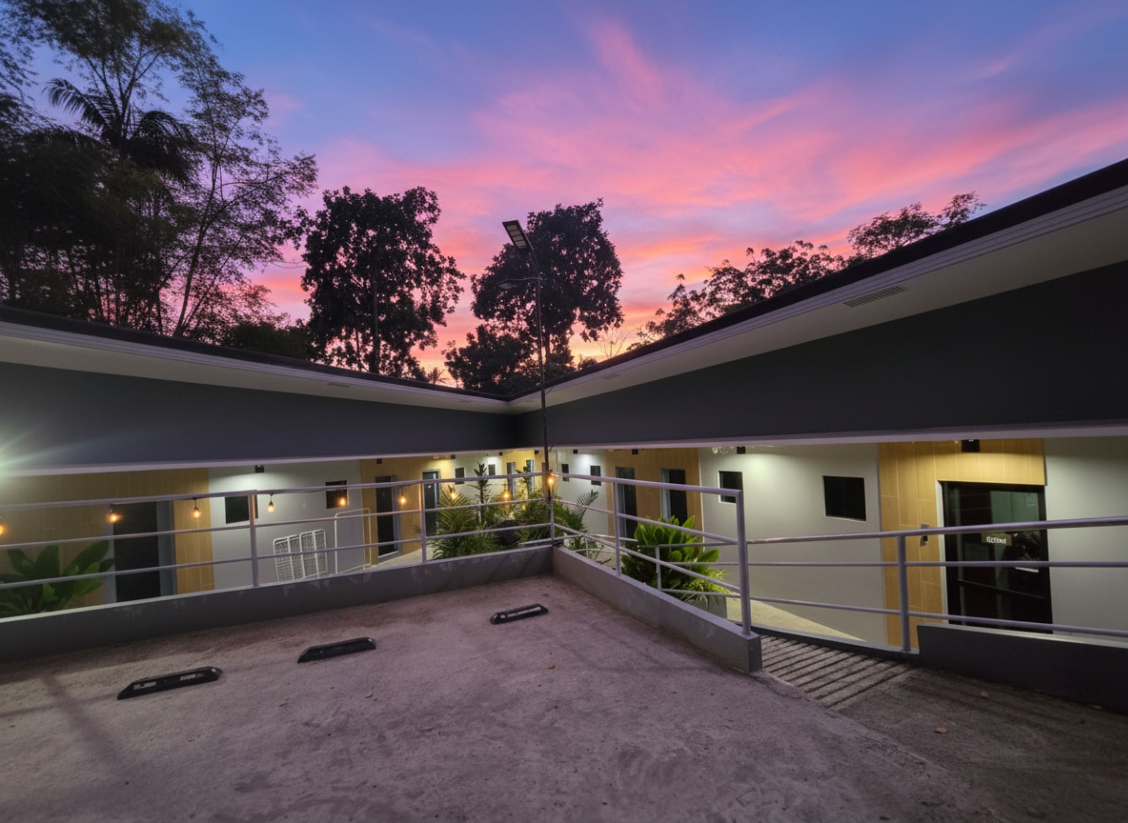 Pátio de hotel com área de estar coberta, escadaria e vista para árvores ao redor.