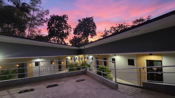 Pátio de hotel com área de estar coberta, escadaria e vista para árvores ao redor.