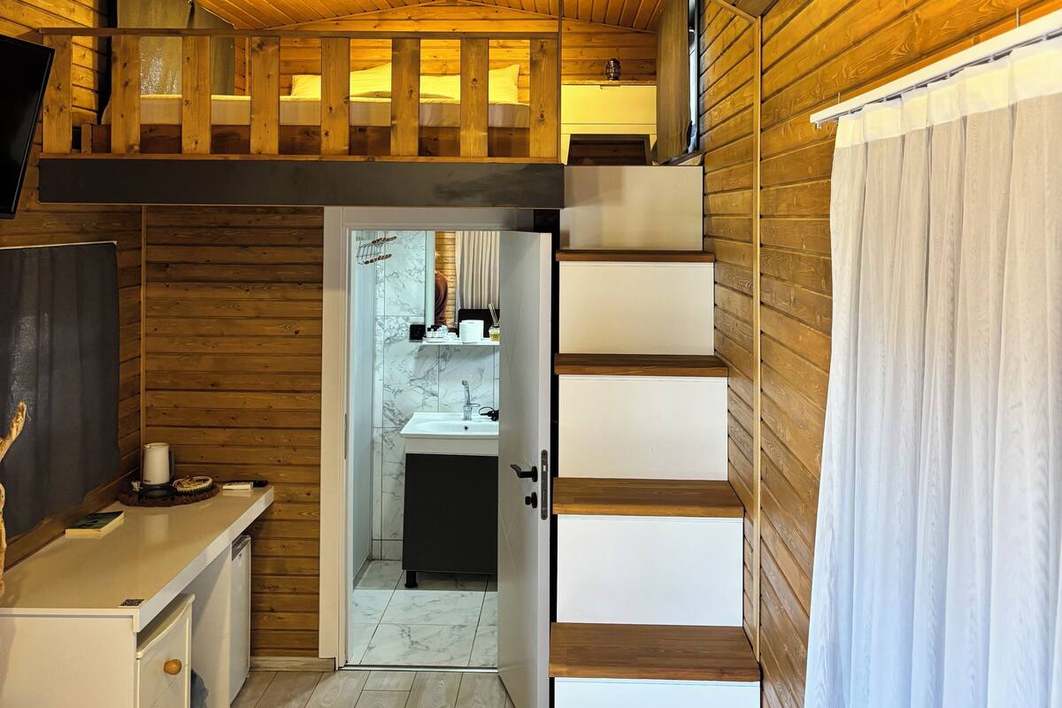 Uma cabana compacta de madeira com um quarto no mezanino, uma kitchenette pequena e um banheiro.