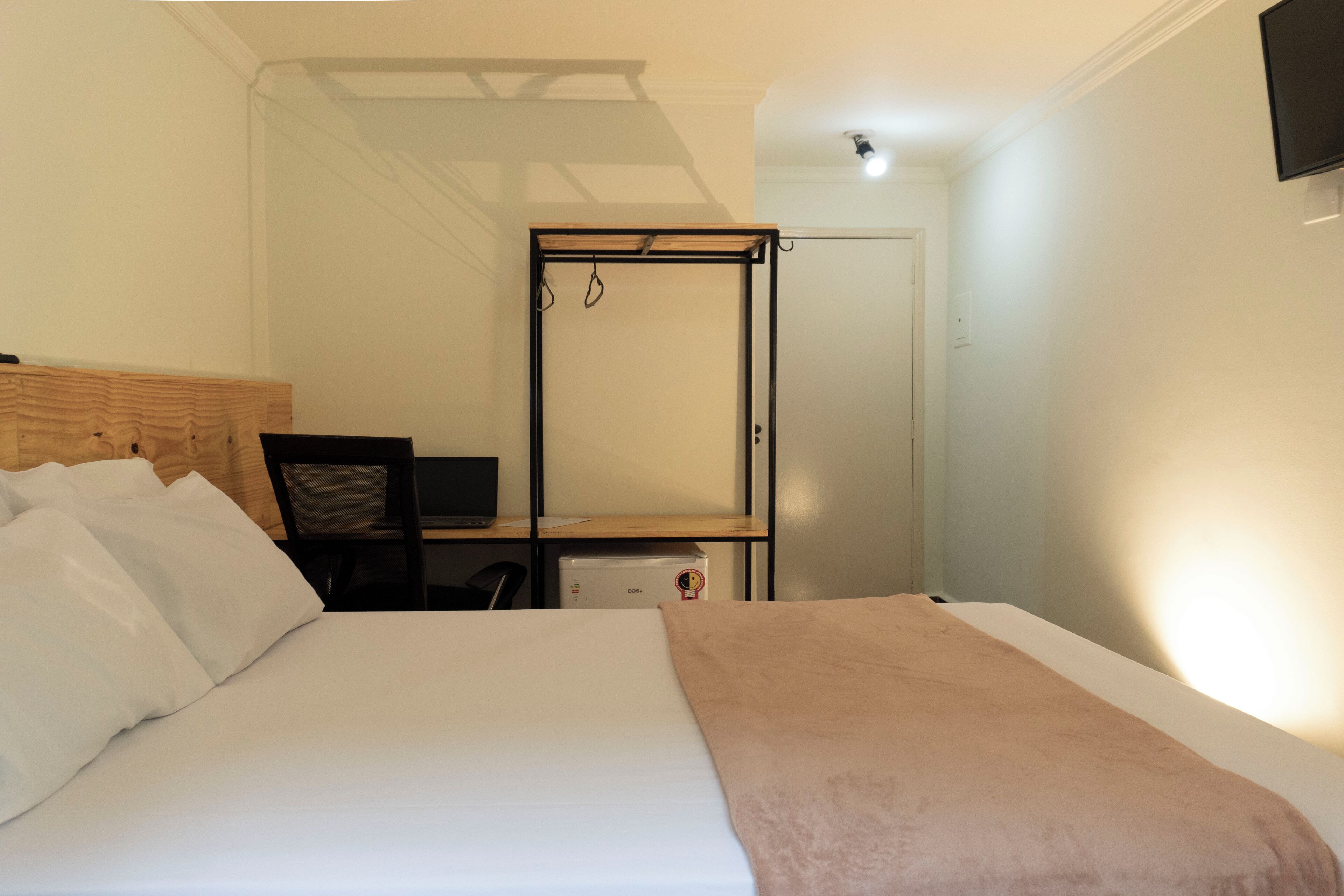 Quarto de hotel com uma cama, uma escrivaninha com computador e um guarda-roupa.