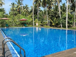 Piscina azul e límpida cercada por palmeiras e folhagem verde.