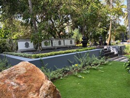  Área de jardim ajardinada com um caminho, uma rocha grande e um muro com detalhes decorativos.