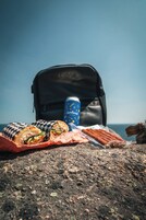 Mochila com uma lata de cerveja Landwash, um sanduíche embalado e uma embalagem de salsichas sobre uma superfície rochosa.