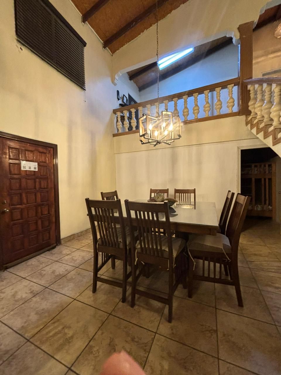 Uma sala de jantar com mesa, cadeiras, um candelabro e uma porta de madeira.
