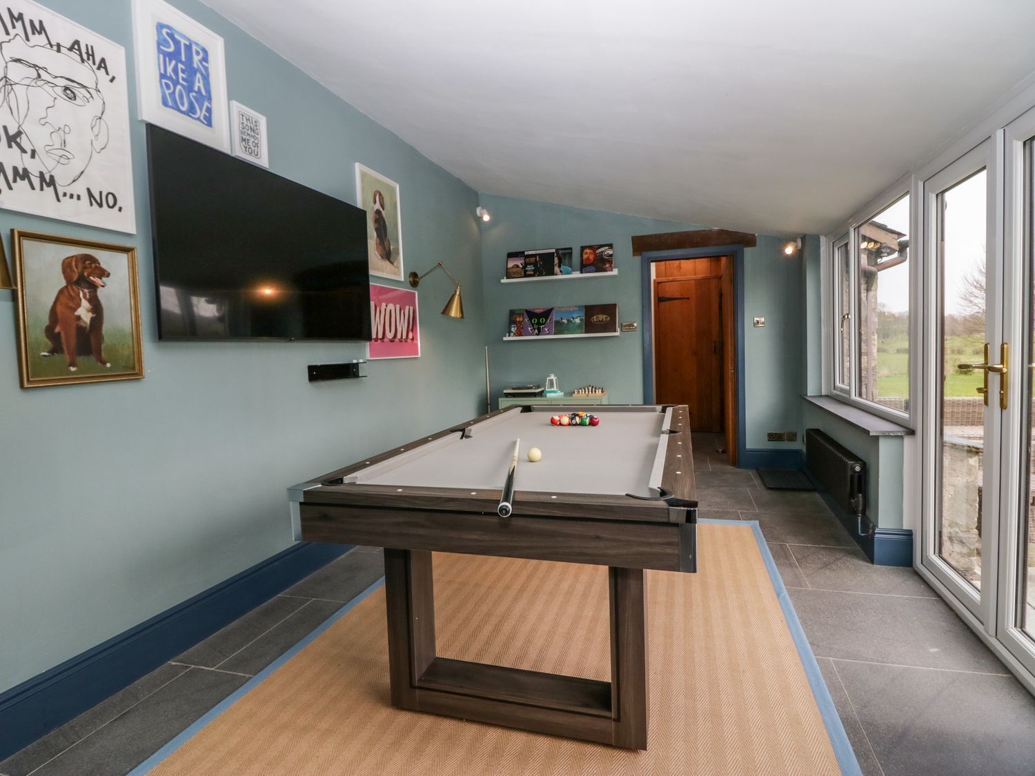 Mesa de bilhar em um quarto com parede azul, quadro com um cachorro e um letreiro que diz 'WOW!'.