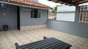Uma área de varanda coberta com piso de azulejos, um banco de madeira e uma janela.