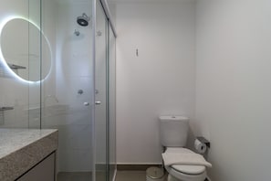 Um banheiro moderno com chuveiro em box de vidro, vaso sanitário e bancada de mármore.